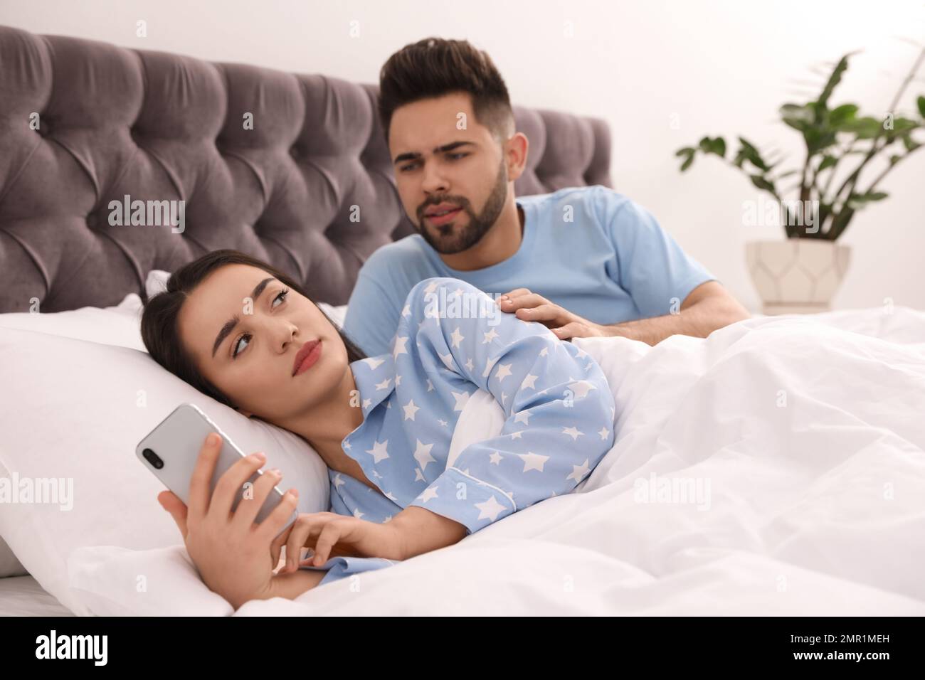 Young woman ignoring her distrustful boyfriend while using smartphone in bed at home Stock Photo ...