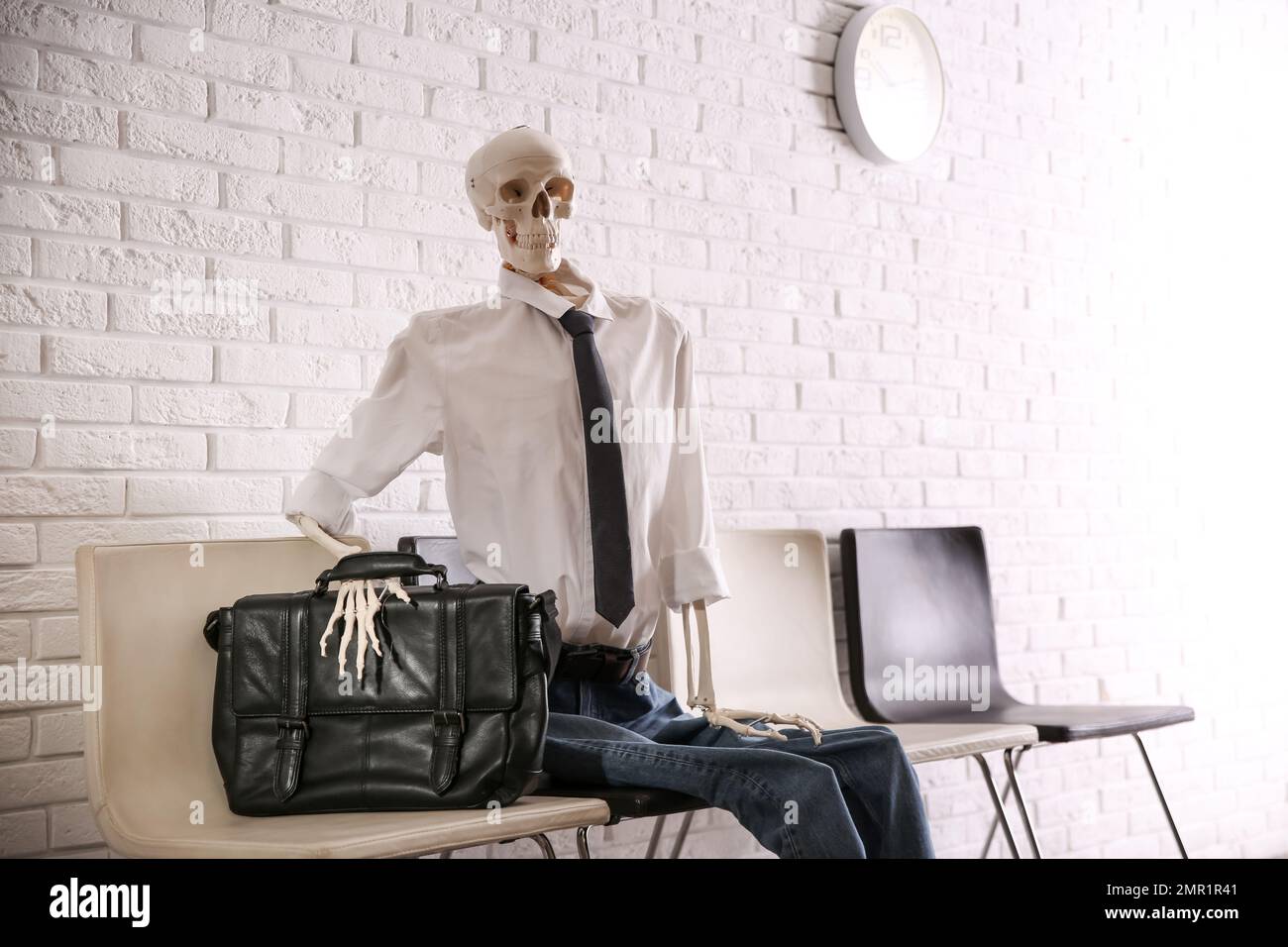 Human skeleton in office wear sitting on chair near brick wall indoors ...