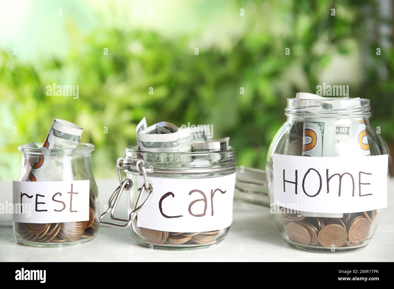 Glass jars with money and tags REST, CAR, HOME on white table against ...