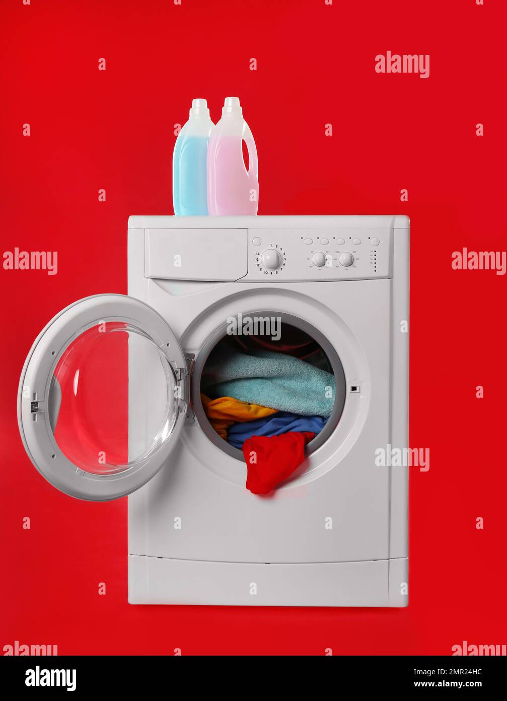 Modern washing machine with laundry and detergents on red background ...
