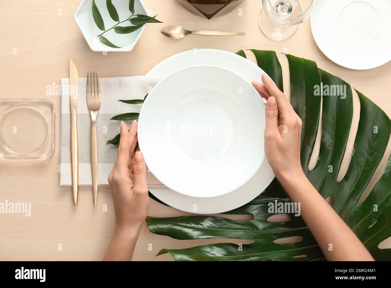 Woman setting table with green leaves for festive dinner, top view ...