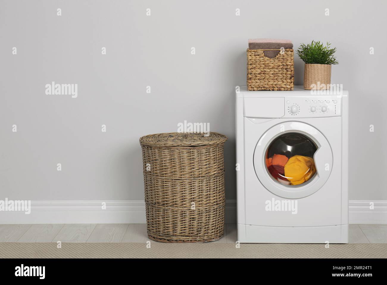 Modern washing machine with laundry, houseplant and wicker baskets near ...