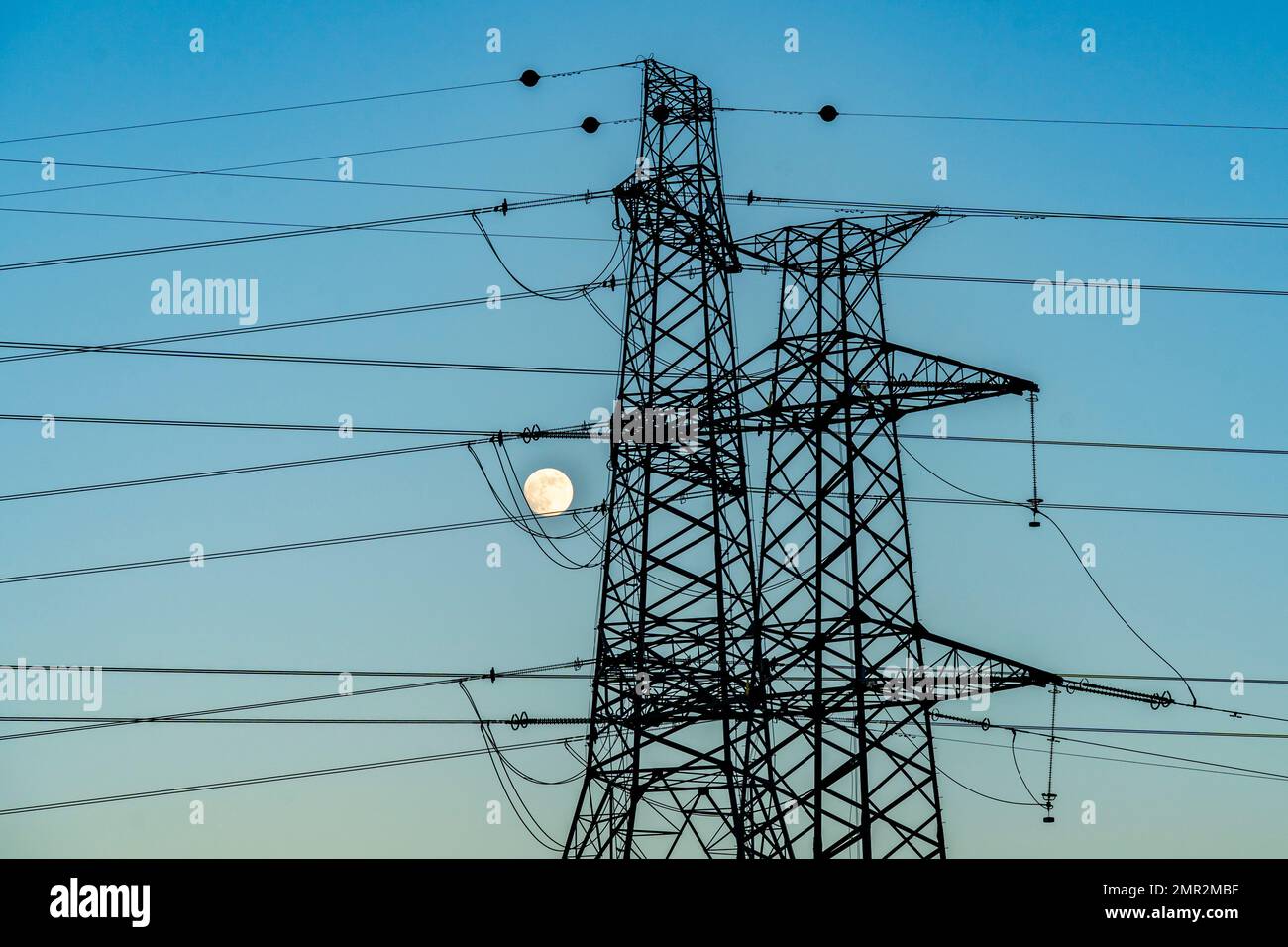Towers of high-voltage transmission lines at sunset with the full moon ...
