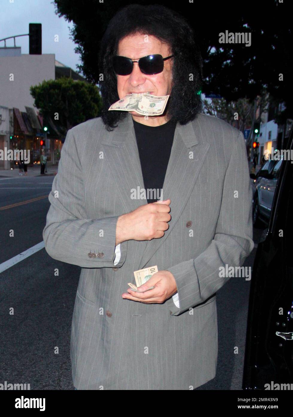 Rock star Gene Simmons playfully chomps down on a 10 dollar bill as he ...