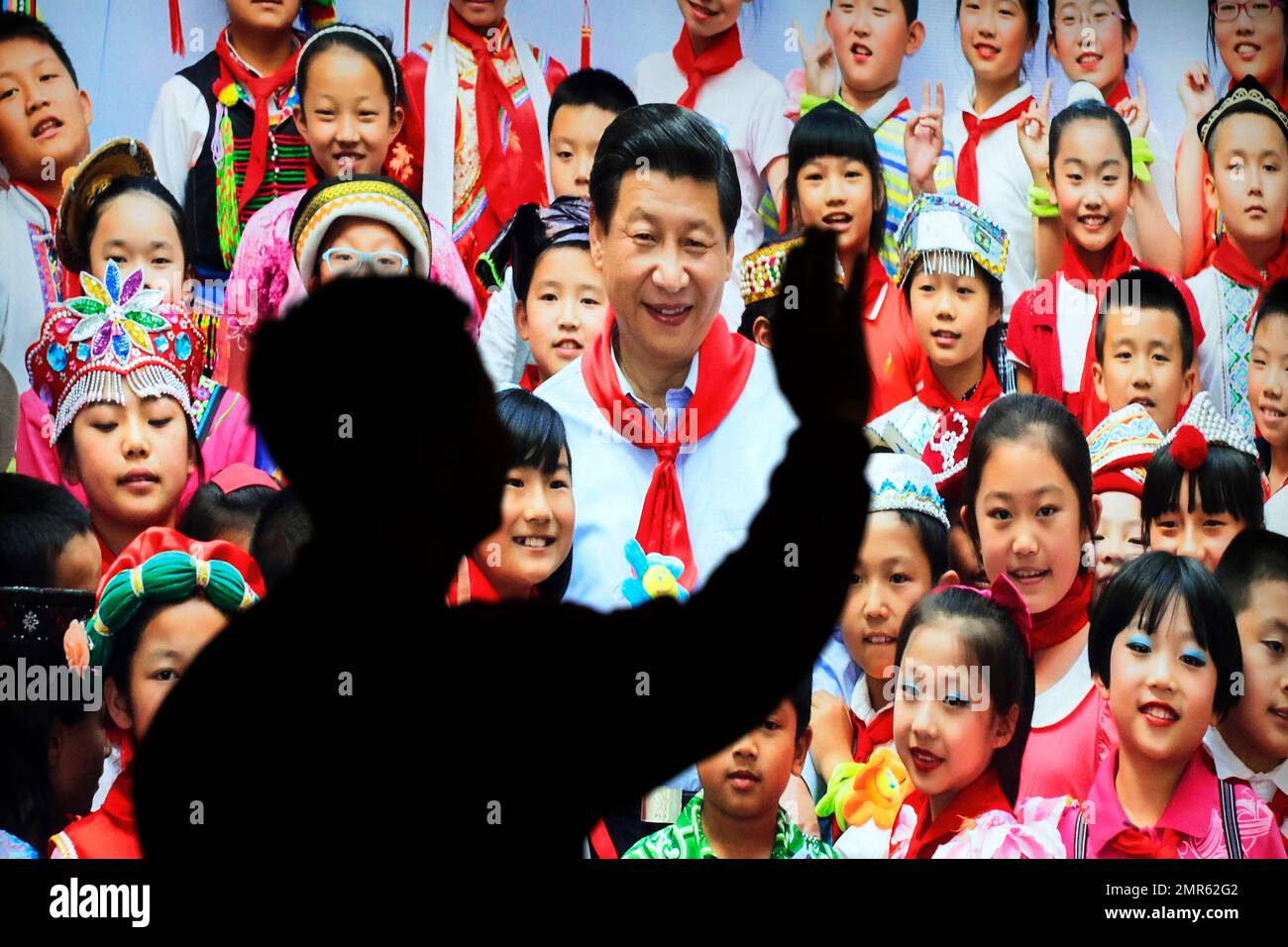 A Chinese man waves in front of a picture showing Chinese President Xi ...
