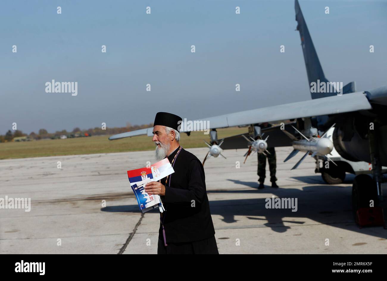 An Orthodox priest holds Serbian flag and passes by a Serbian Army MiG ...