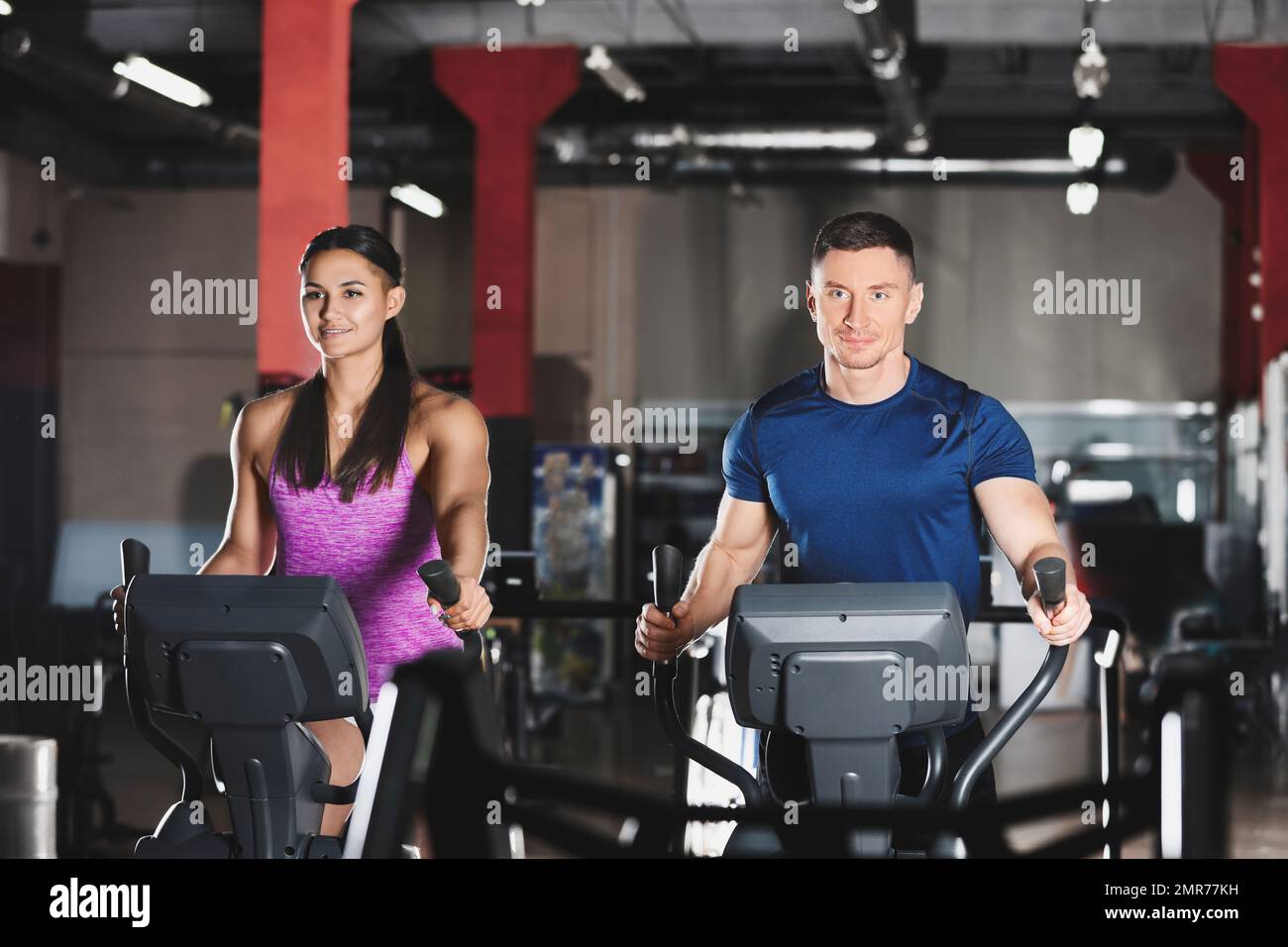 Couple working out on elliptical trainers in gym Stock Photo - Alamy
