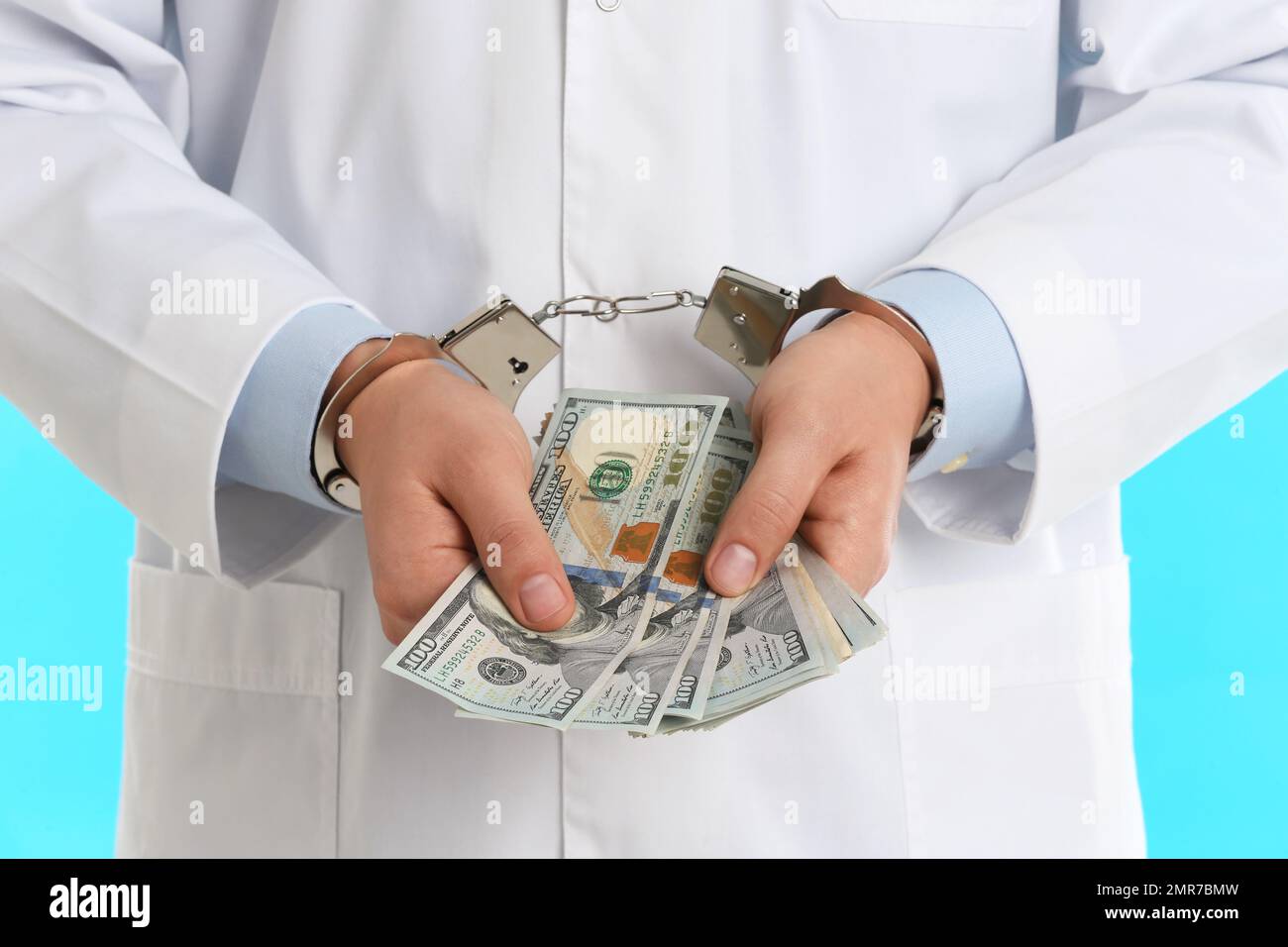 Doctor in handcuffs with bribe on light blue background, closeup ...