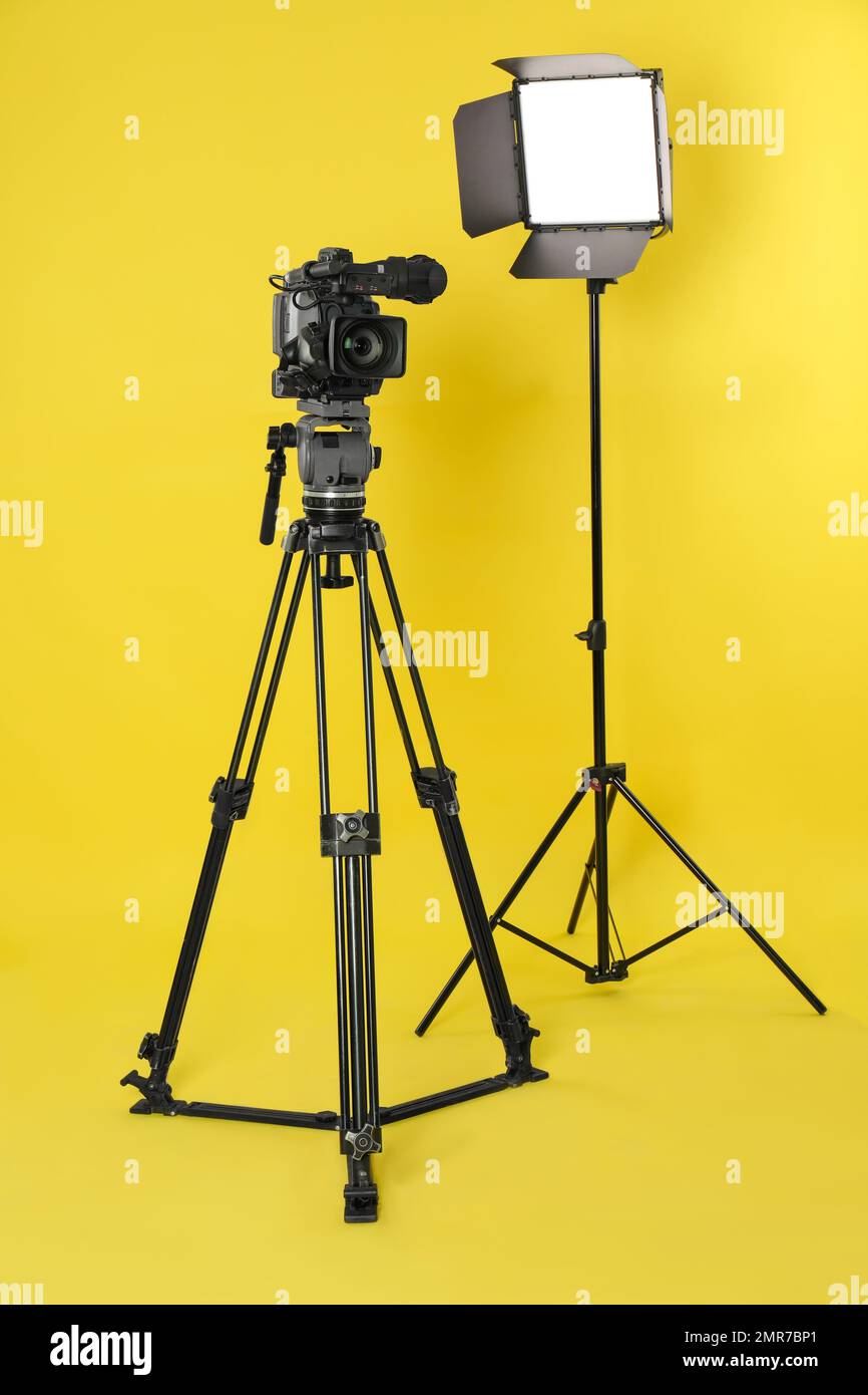 Professional video camera and lighting equipment on yellow background ...