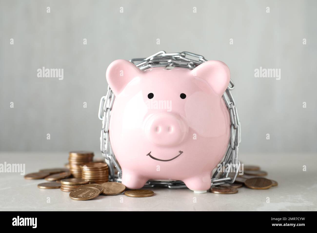 Piggy bank with steel chain and coins on grey marble table. Money ...