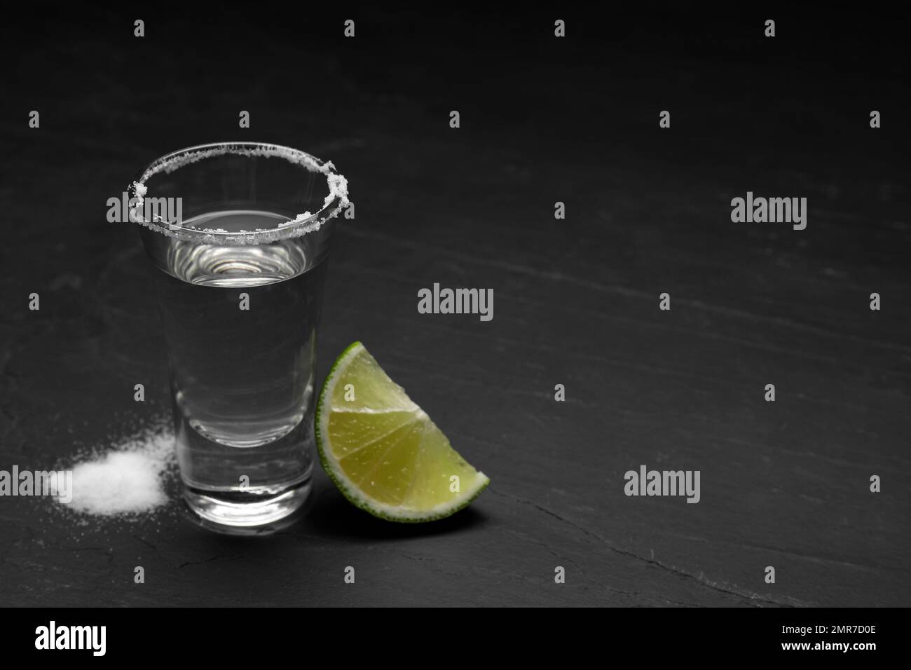 Mexican Tequila shot with salt and lime slice on black table. Space for ...
