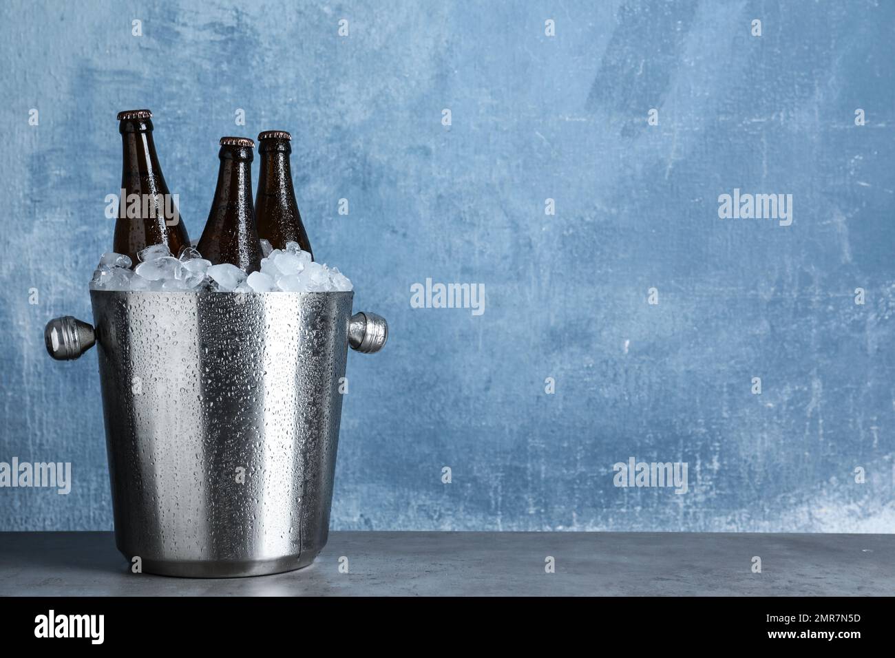 Beer in metal bucket with ice on grey table against light blue ...