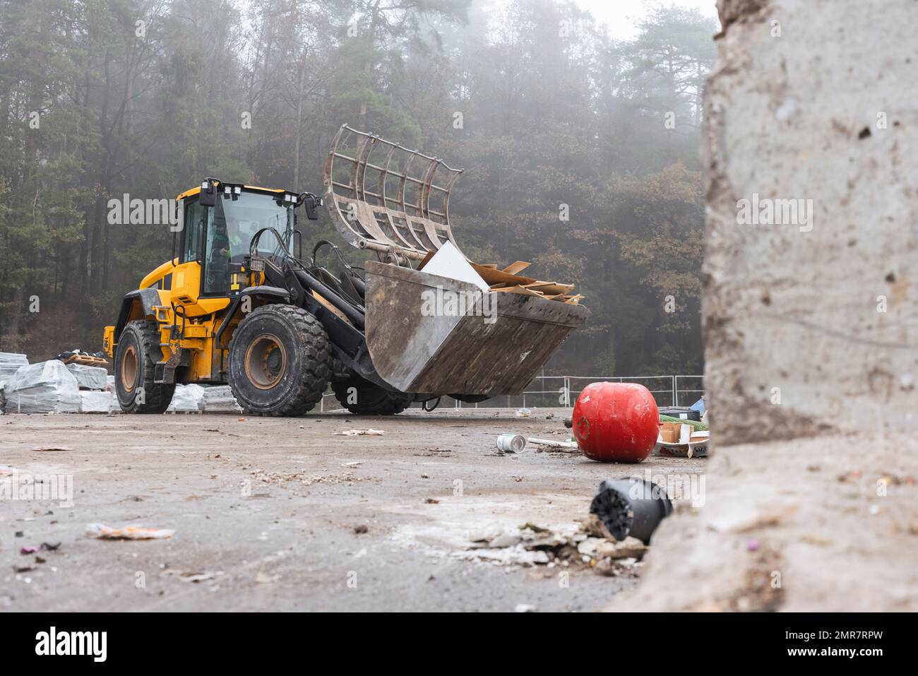 Yellow wheel loader, with lifted scrap grapple, moving along the ...