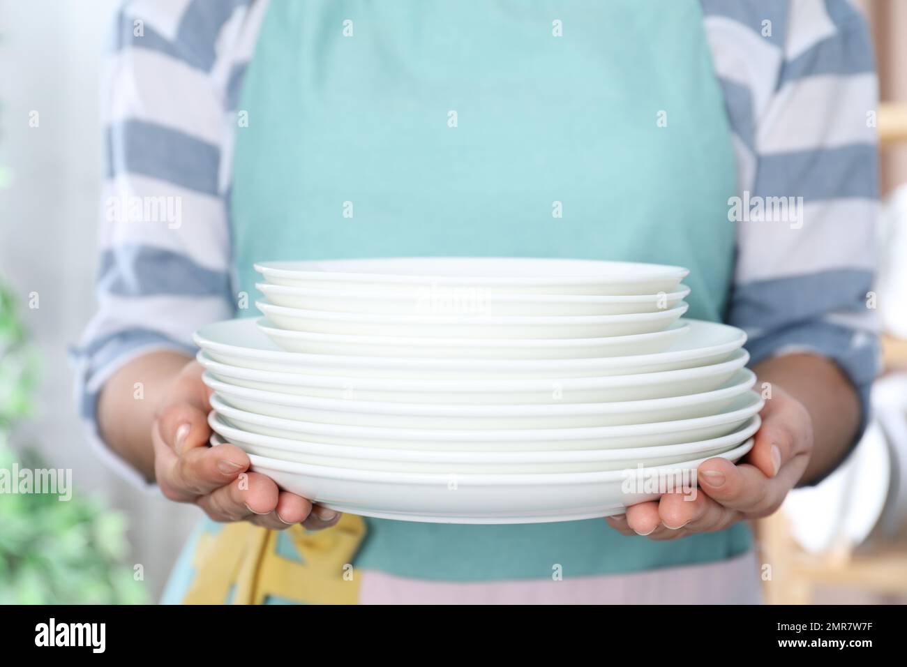 Woman holding stack of clean plates on blurred background, closeup ...
