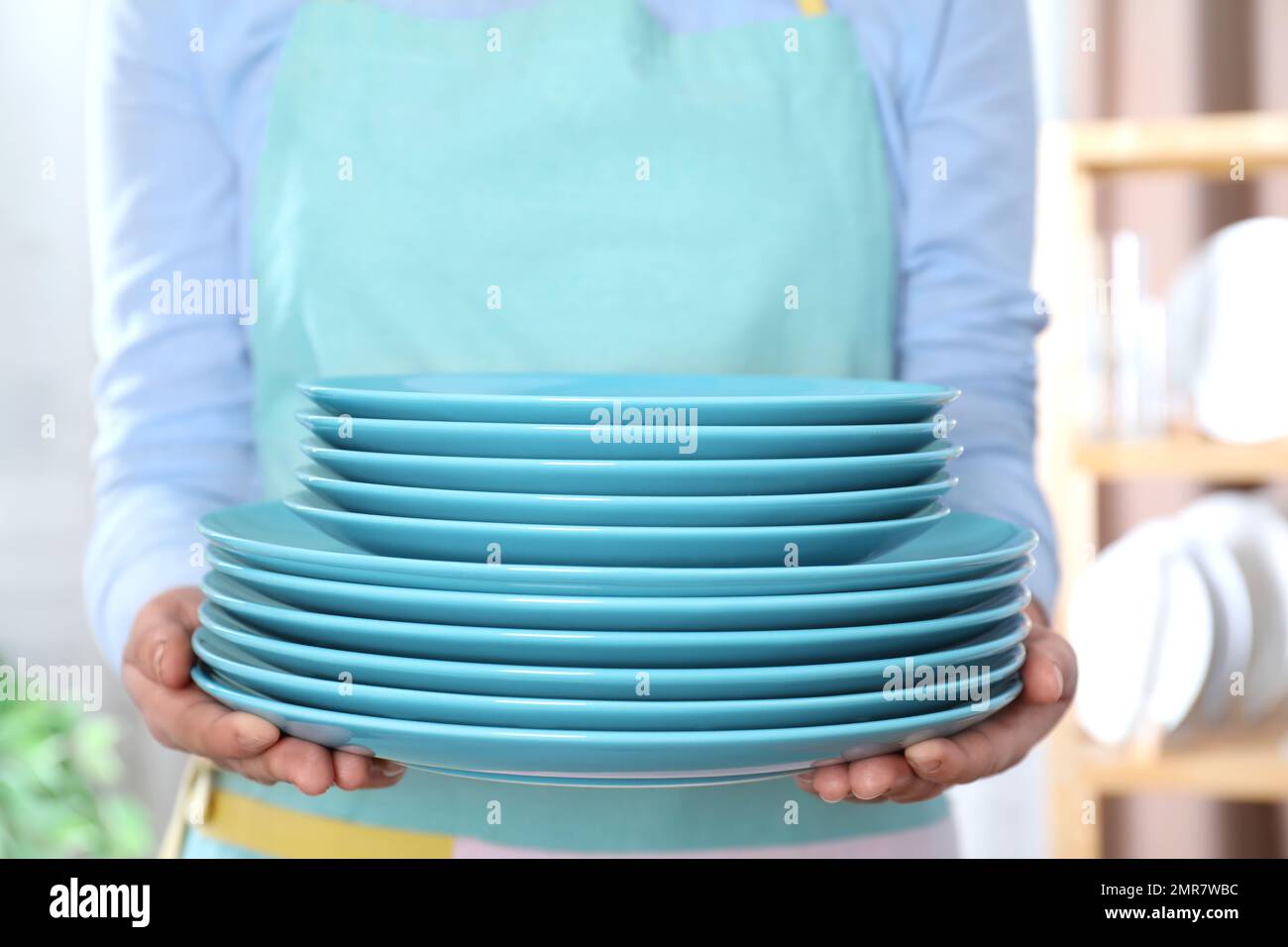 Woman holding stack of clean plates on blurred background, closeup ...