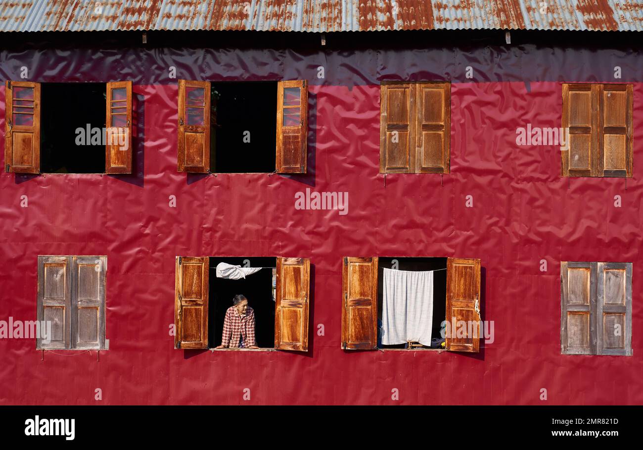 A woman looking out of the window of an old red house with worn wooden ...