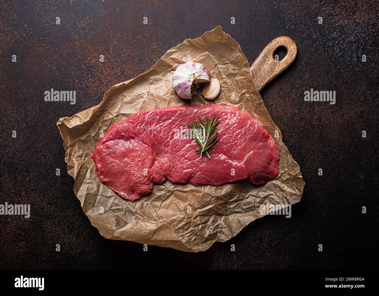 Beef lean raw fillet steak on baking paper with rosemary, garlic and spices on dark brown rustic ...