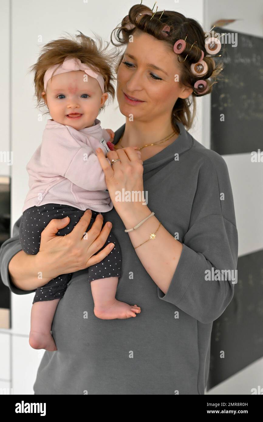 Mother with curlers in her hair, cuddling with daughter, infant ...