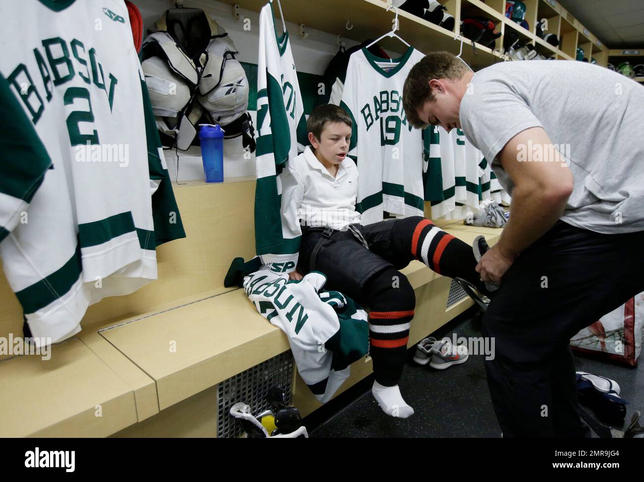 Coleman Walsh, 10, of Walpole, Mass., left, is assisted with his skates ...