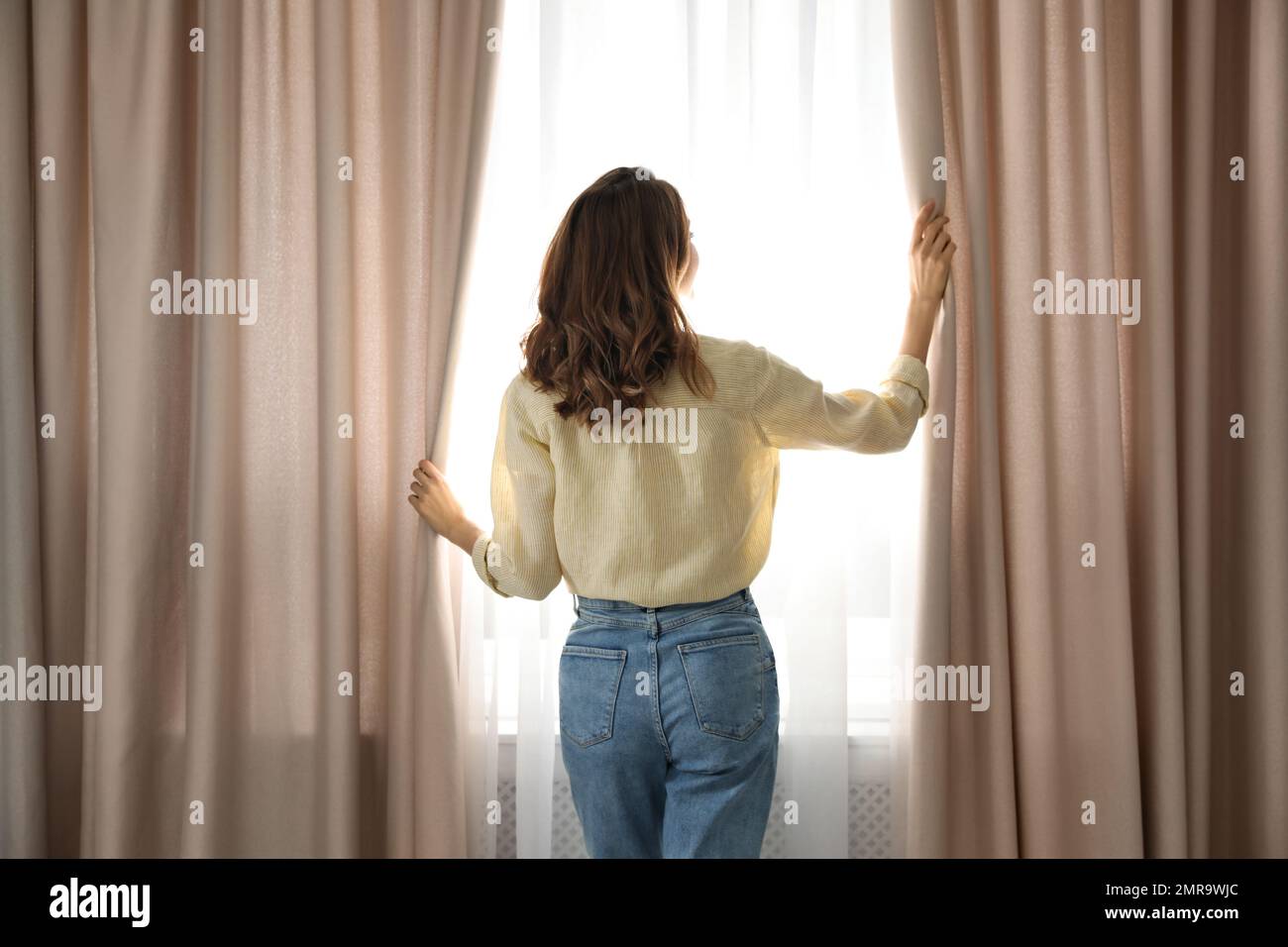 Woman opening window curtains at home in morning, back view Stock Photo ...