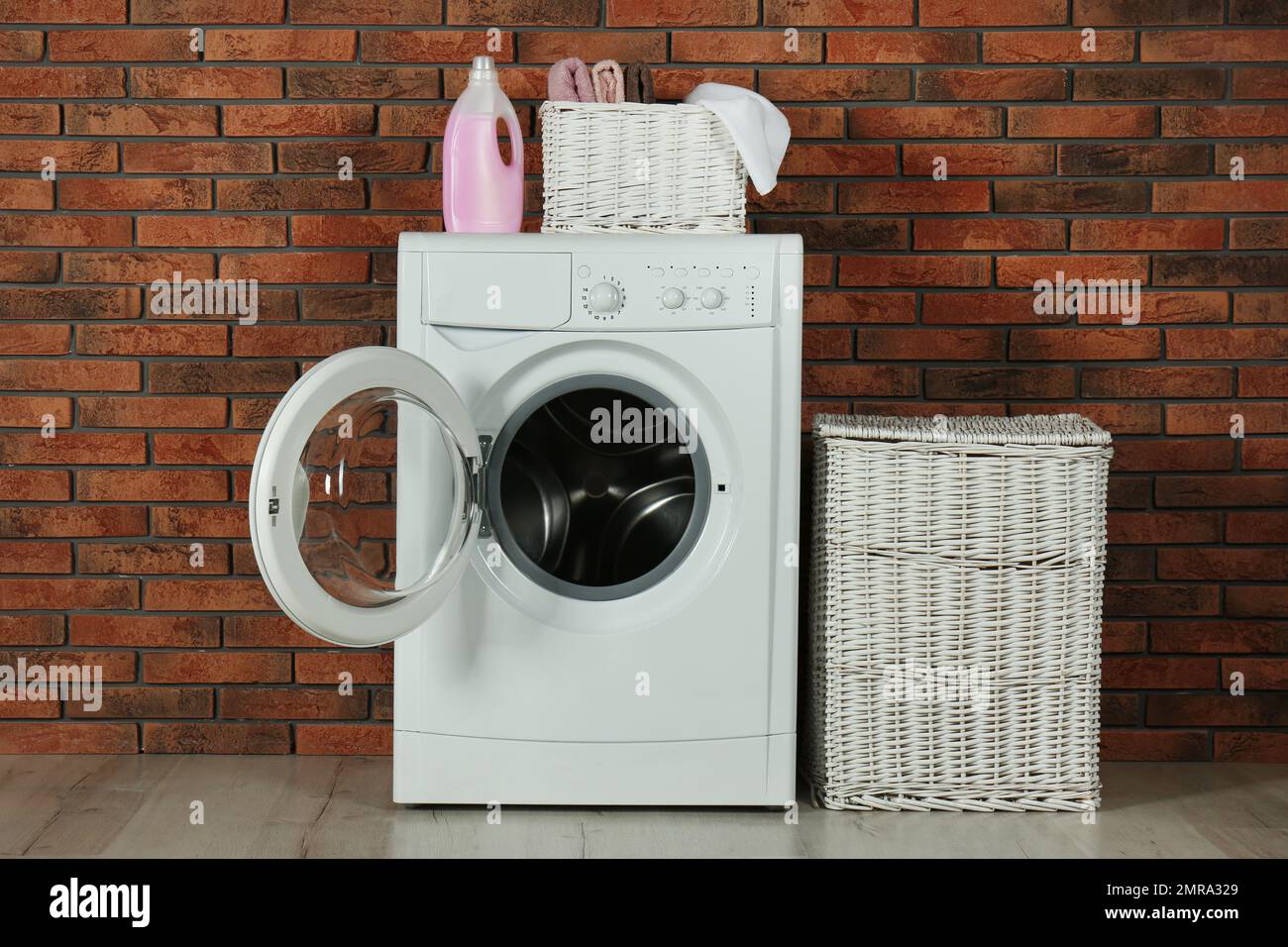 Modern washing machine with detergent and laundry baskets near brick ...