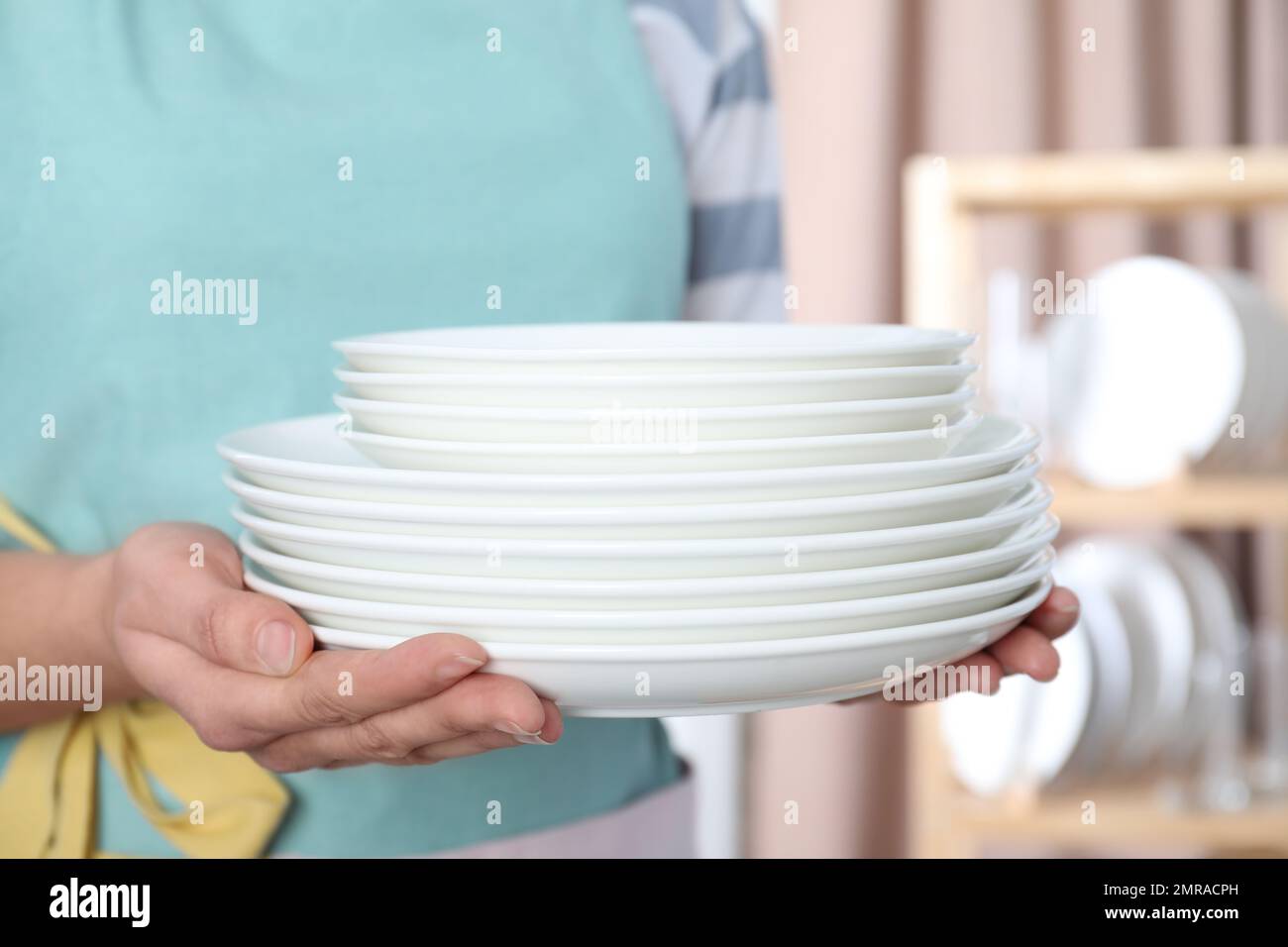 Woman holding stack of clean plates on blurred background, closeup ...