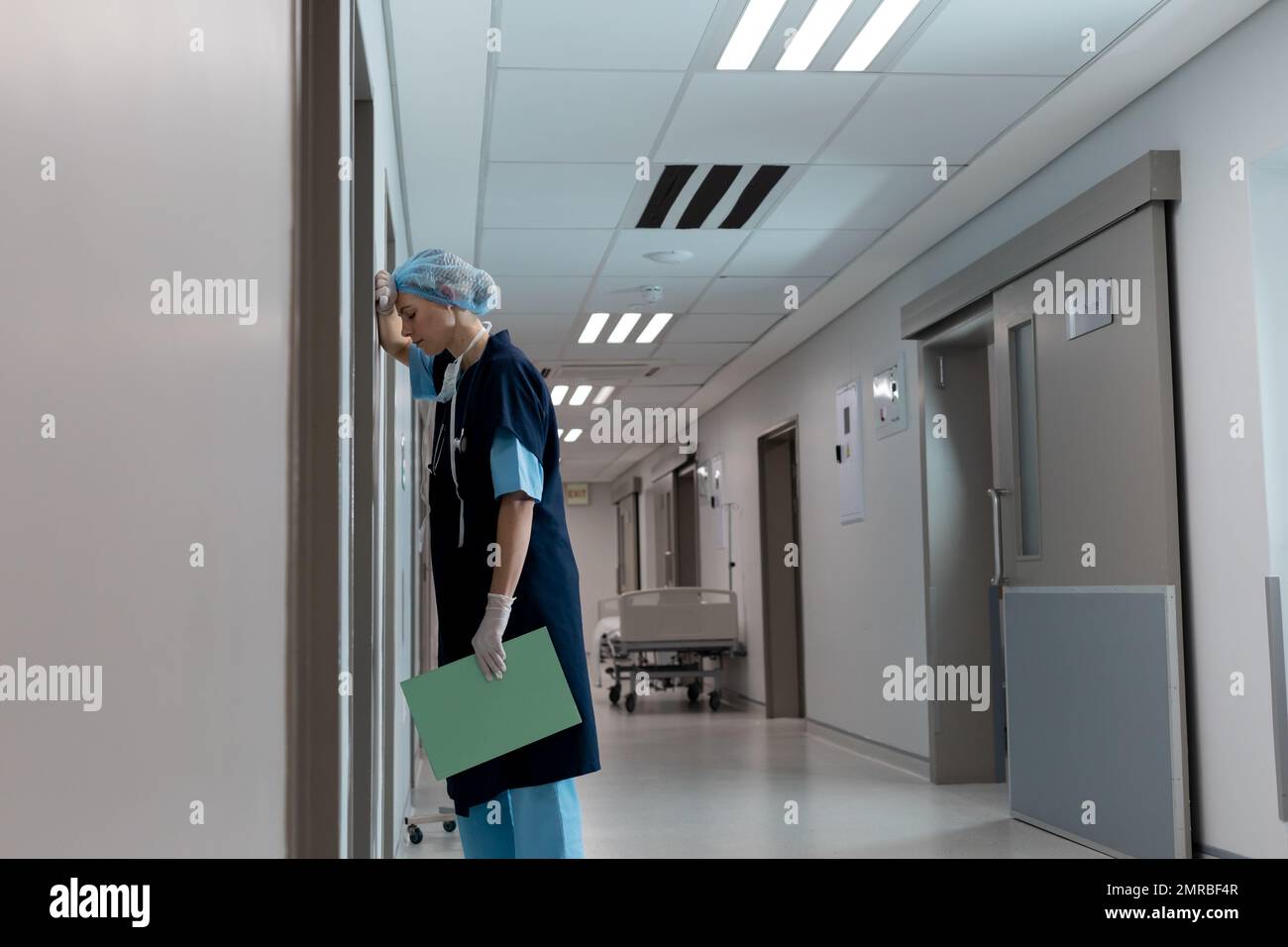 Tired caucasian female doctor wearing hair net in hospital corridor ...