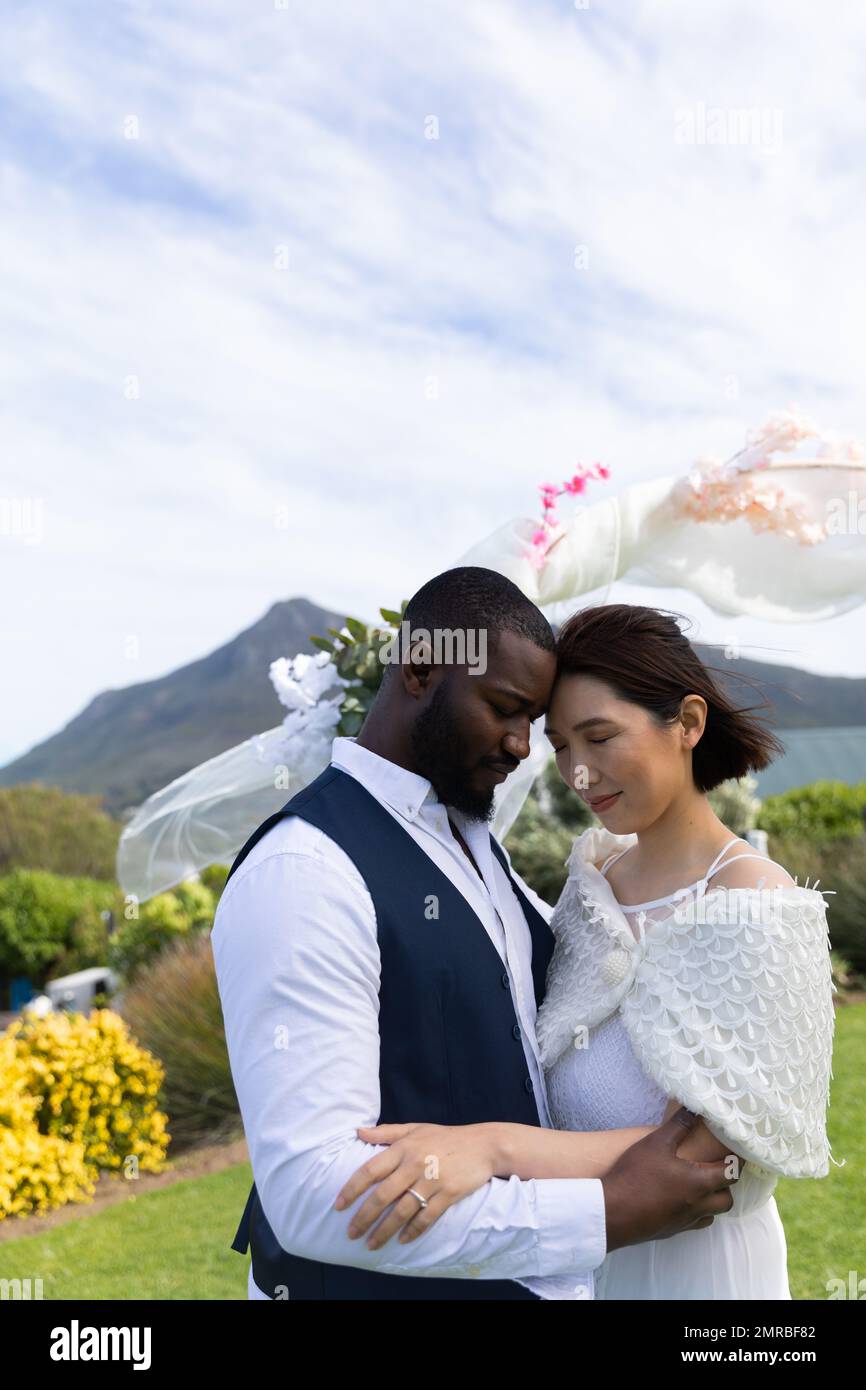 Vertical of happy, diverse bride and groom embracing with eyes closed ...