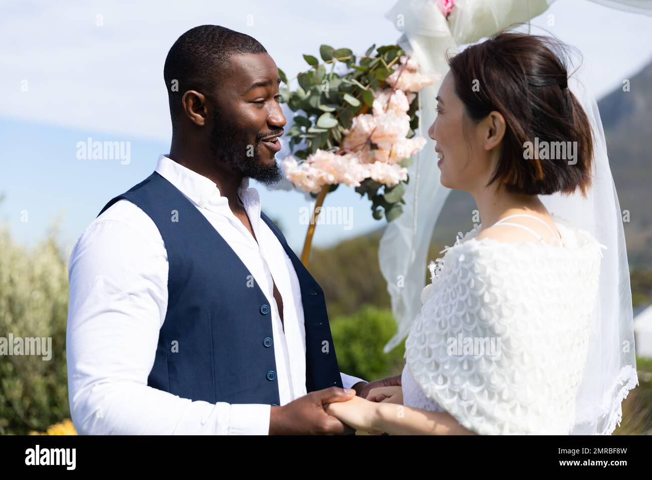 Happy, diverse bride and groom holding hands, making marriage vows at ...