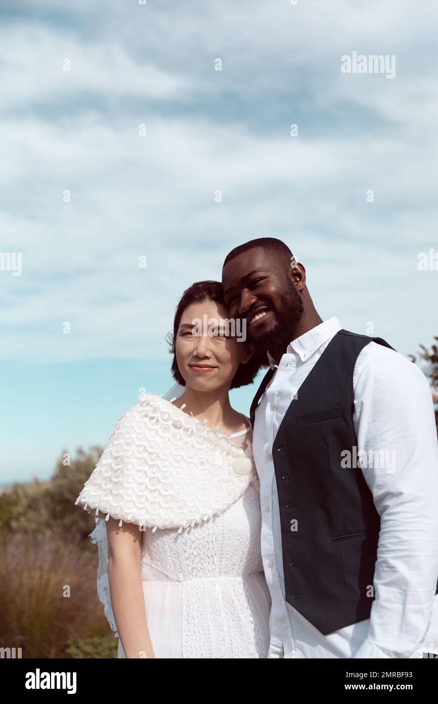 Vertical of happy, diverse bride and groom embracing and smiling at ...