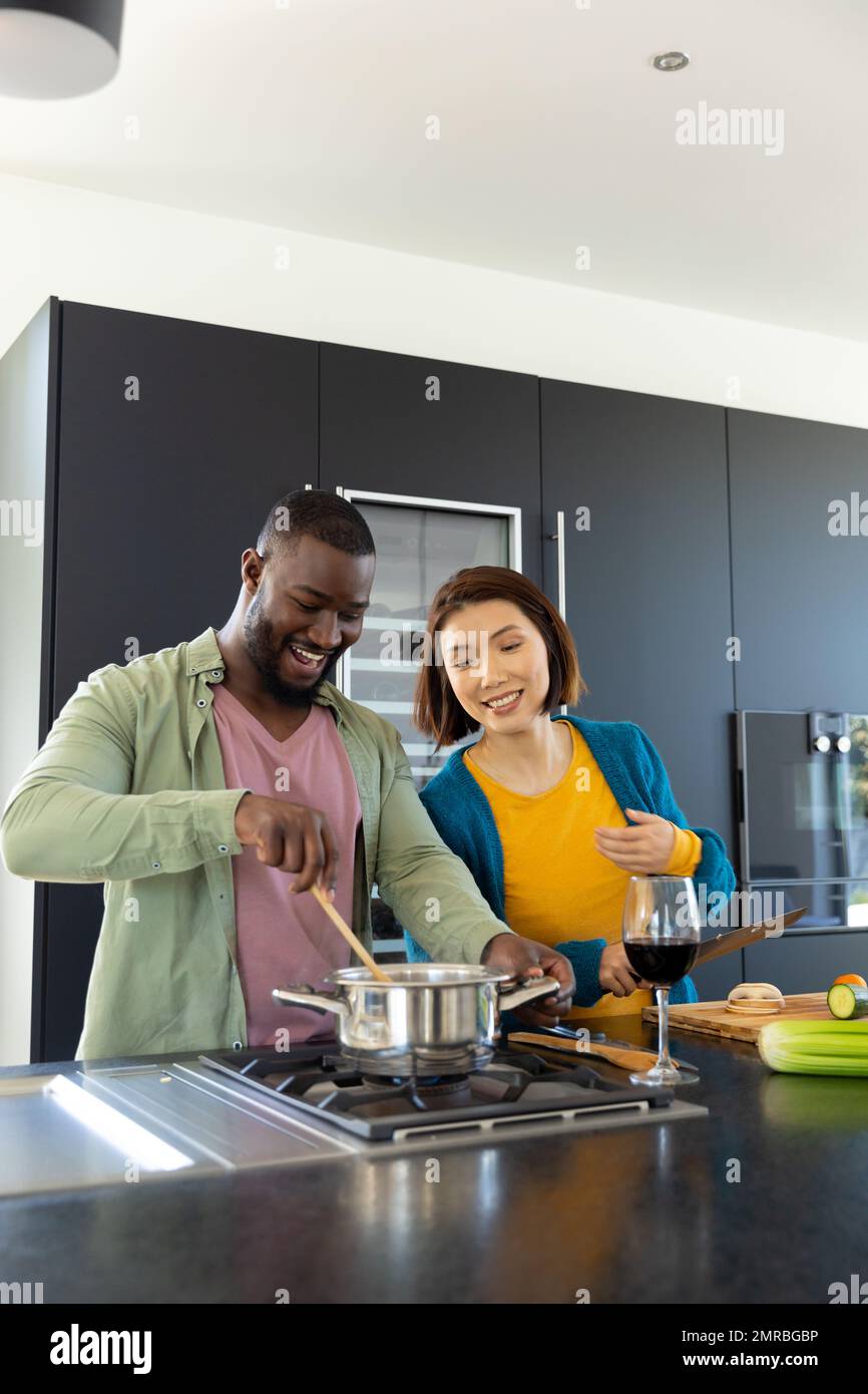 Vertical of happy diverse couple cooking together in modern kitchen ...