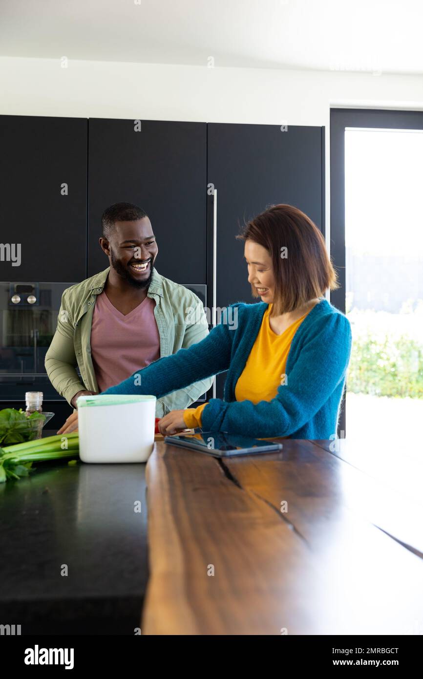 Vertical of happy diverse couple cooking, using tablet and composting ...