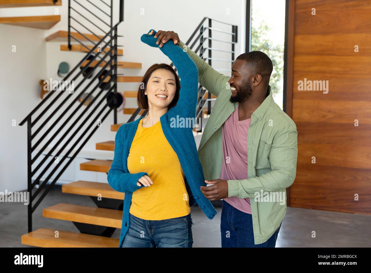 Happy diverse couple having fun dancing together in hallway at home ...