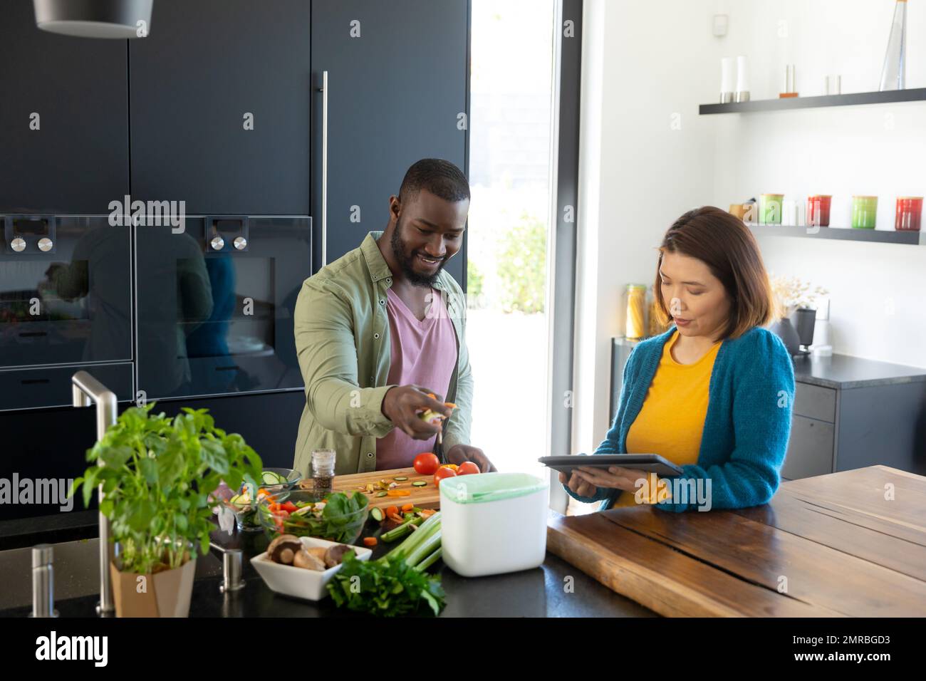 Happy diverse couple cooking together, using tablet and composting ...