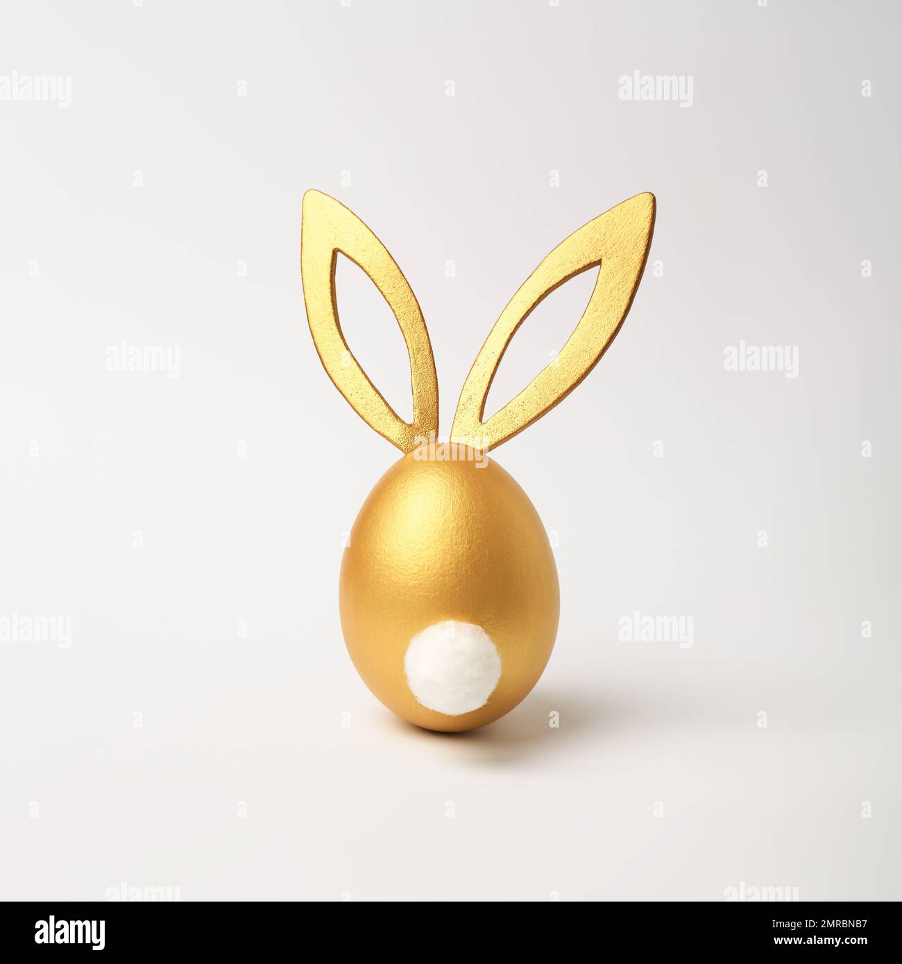 Golden Easter egg with bunny ears and tail on white background. Minimal ...
