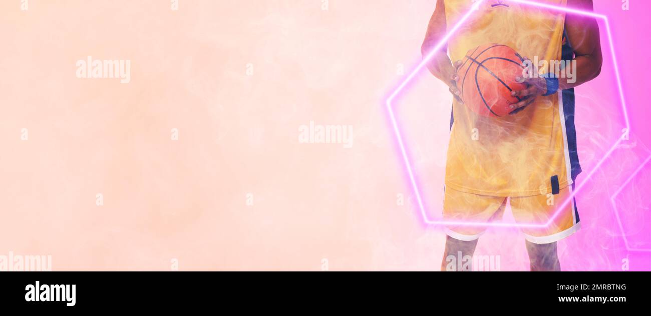 Midsection of biracial male player holding basketball by glowing ...