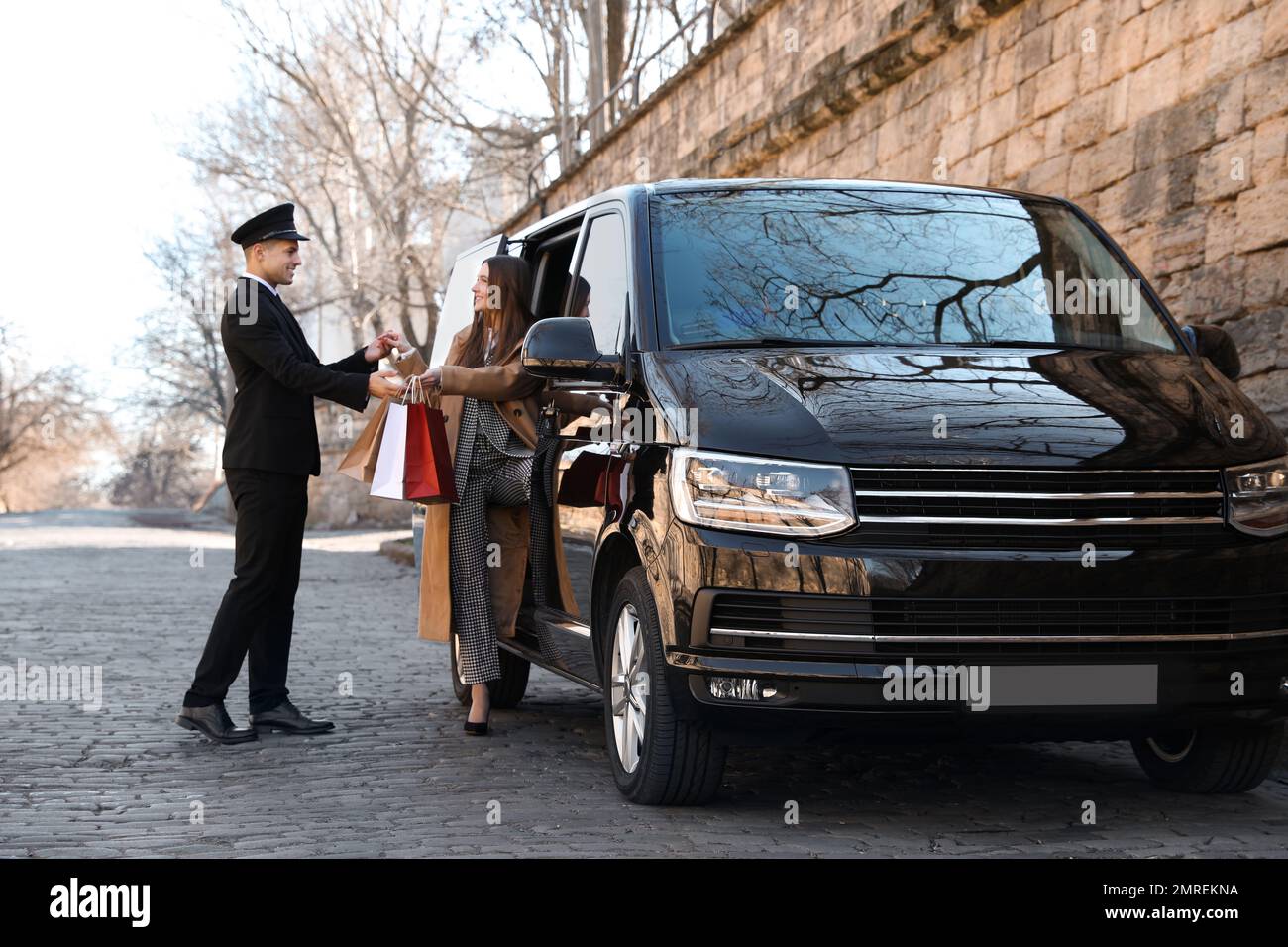 Professional driver helping woman with shopping bags to get out of car ...