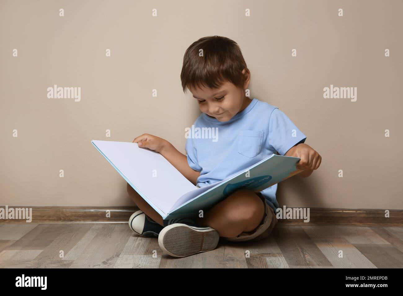 Cute little boy reading book on floor near beige wall Stock Photo - Alamy