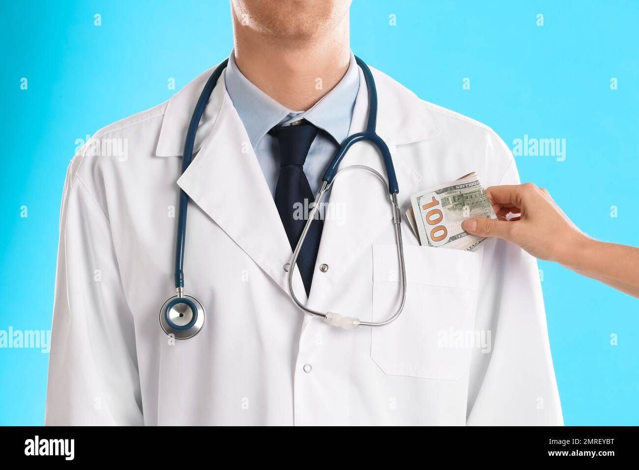 Patient putting bribe into doctor's pocket on light blue background ...