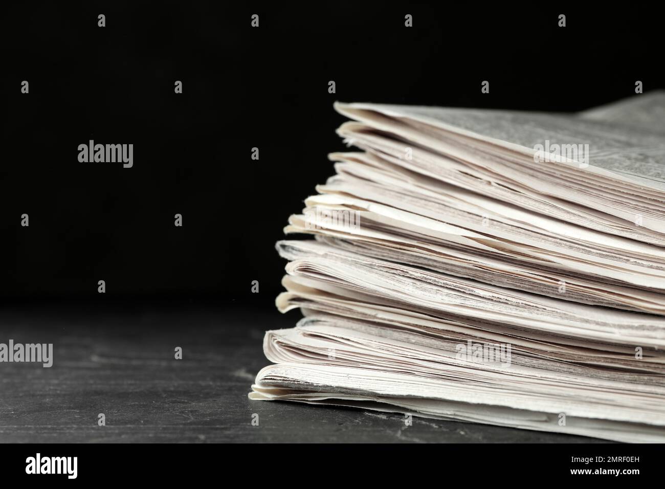 Stack of newspapers on dark stone table, space for text. Journalist's ...