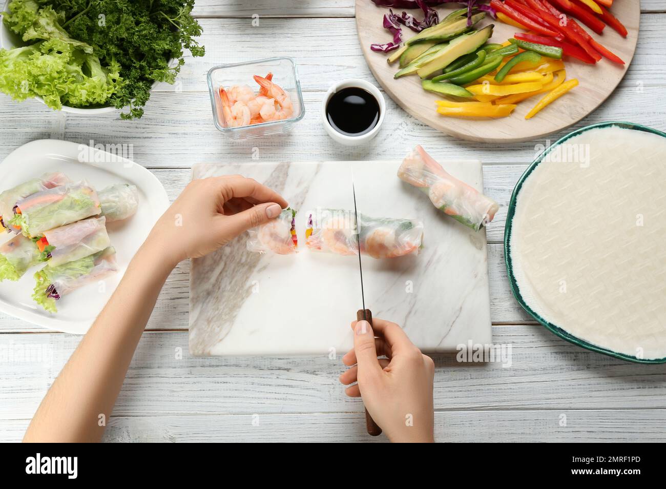 Woman cutting rice paper roll at white wooden table, top view Stock ...