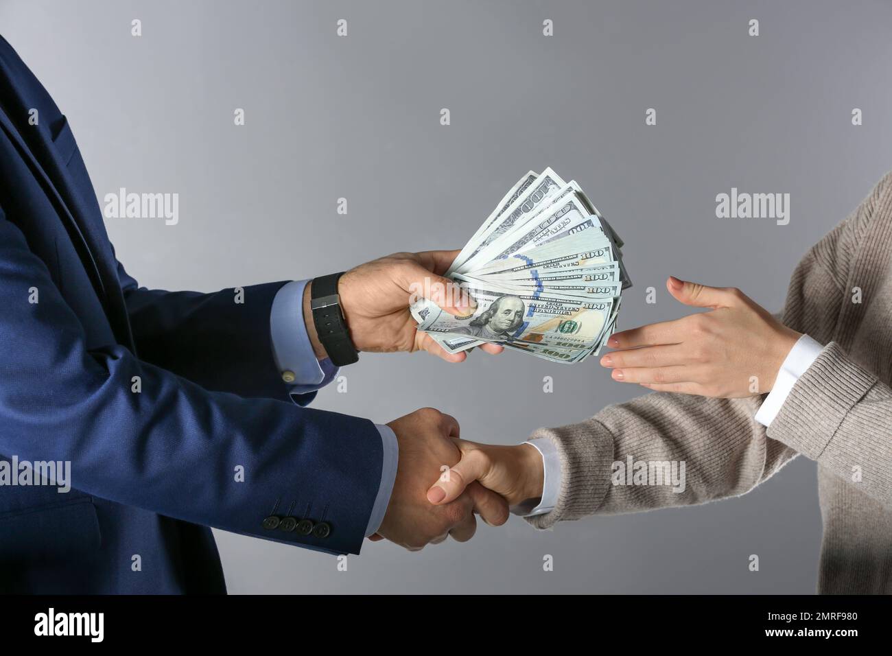 Man shaking hands with woman and offering bribe on grey background ...