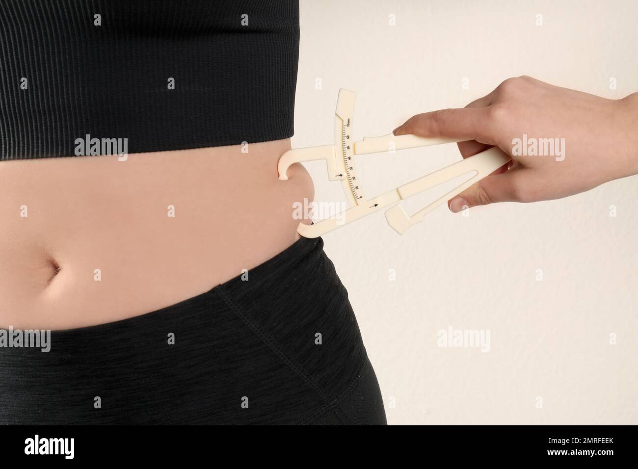 Nutritionist measuring woman's body fat layer with caliper on beige ...