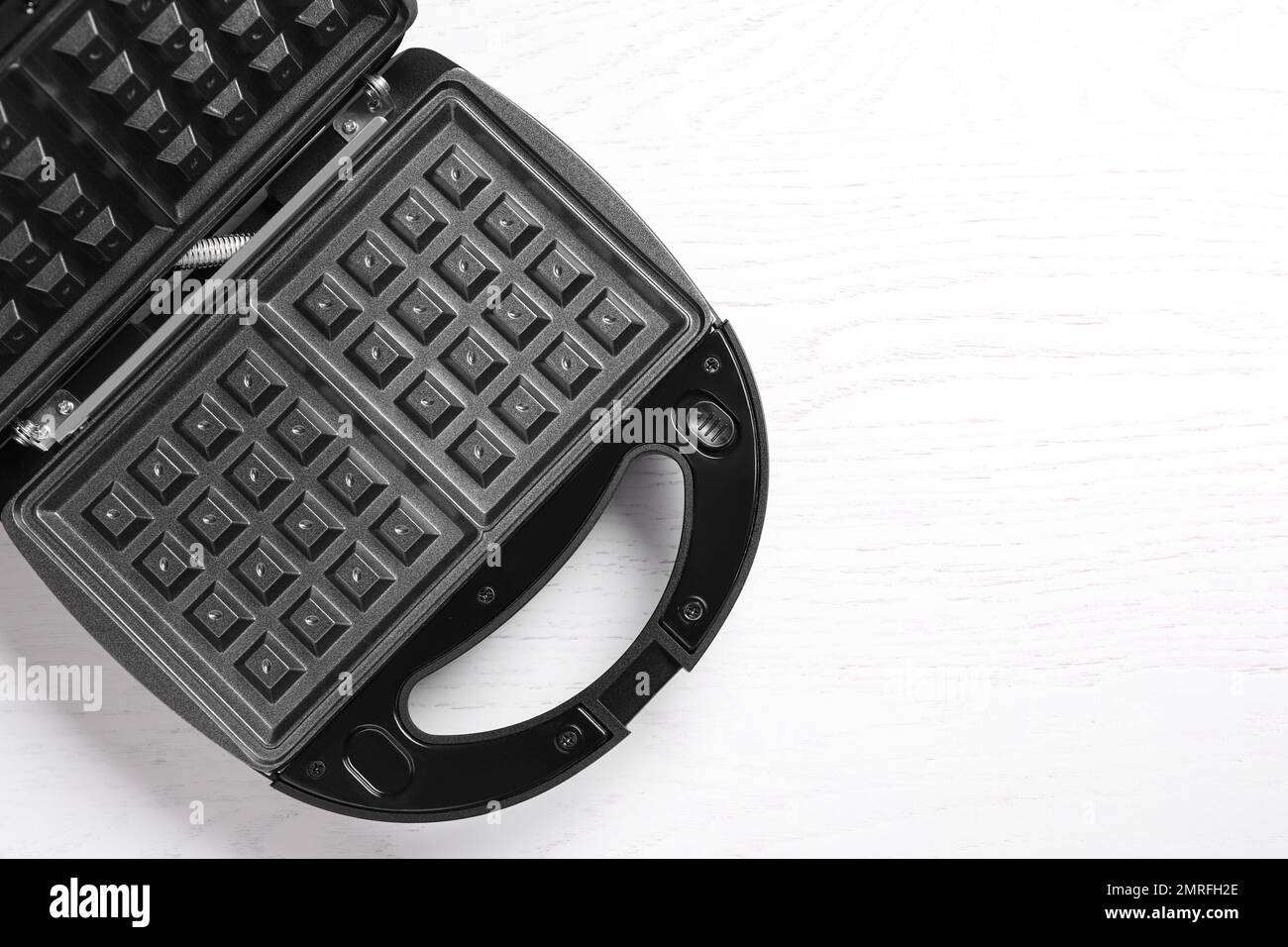 Modern waffle iron on white wooden table, top view. Space for text ...