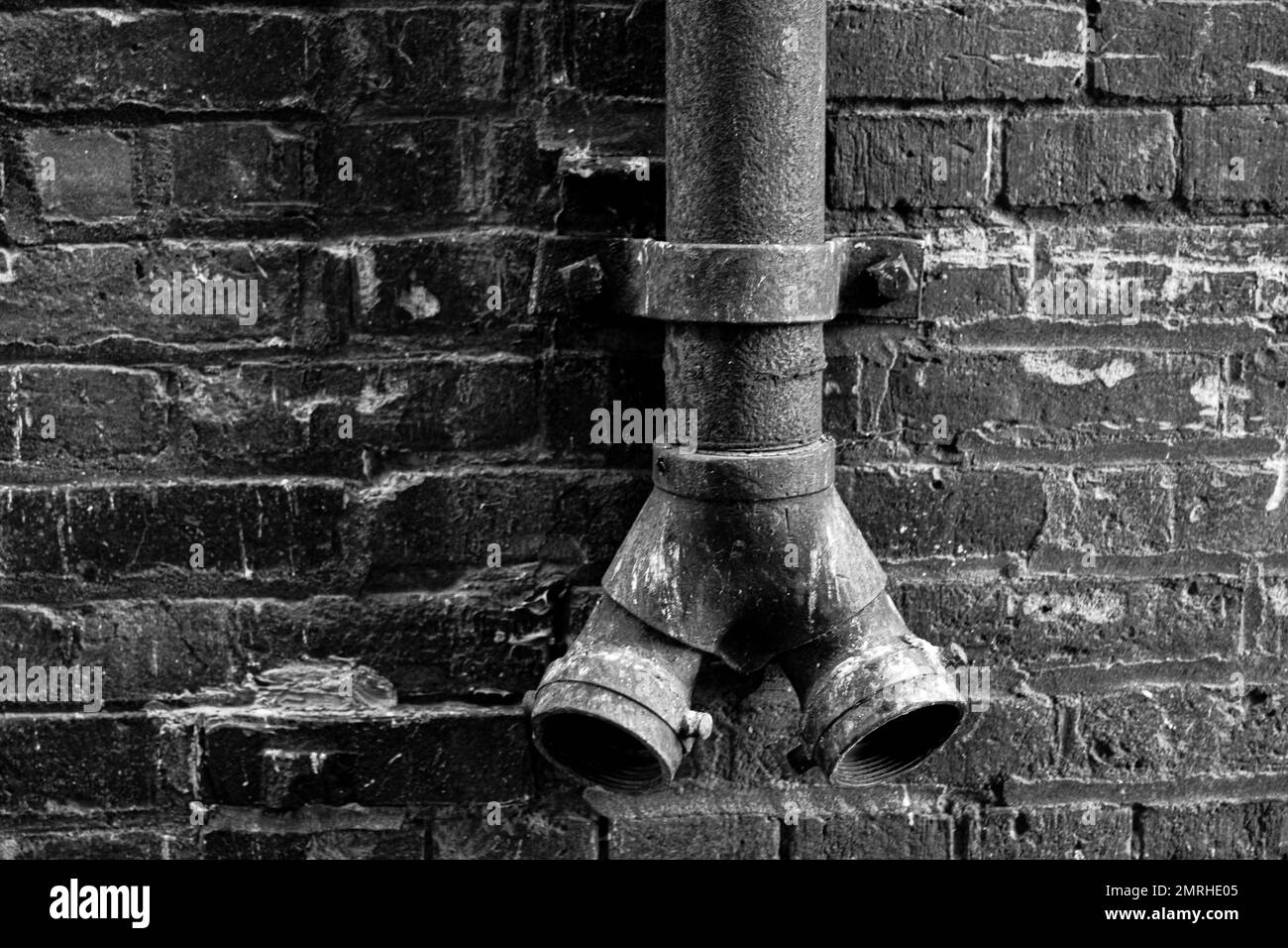 A grayscale of an old rain spigot in an alley with a wall background ...