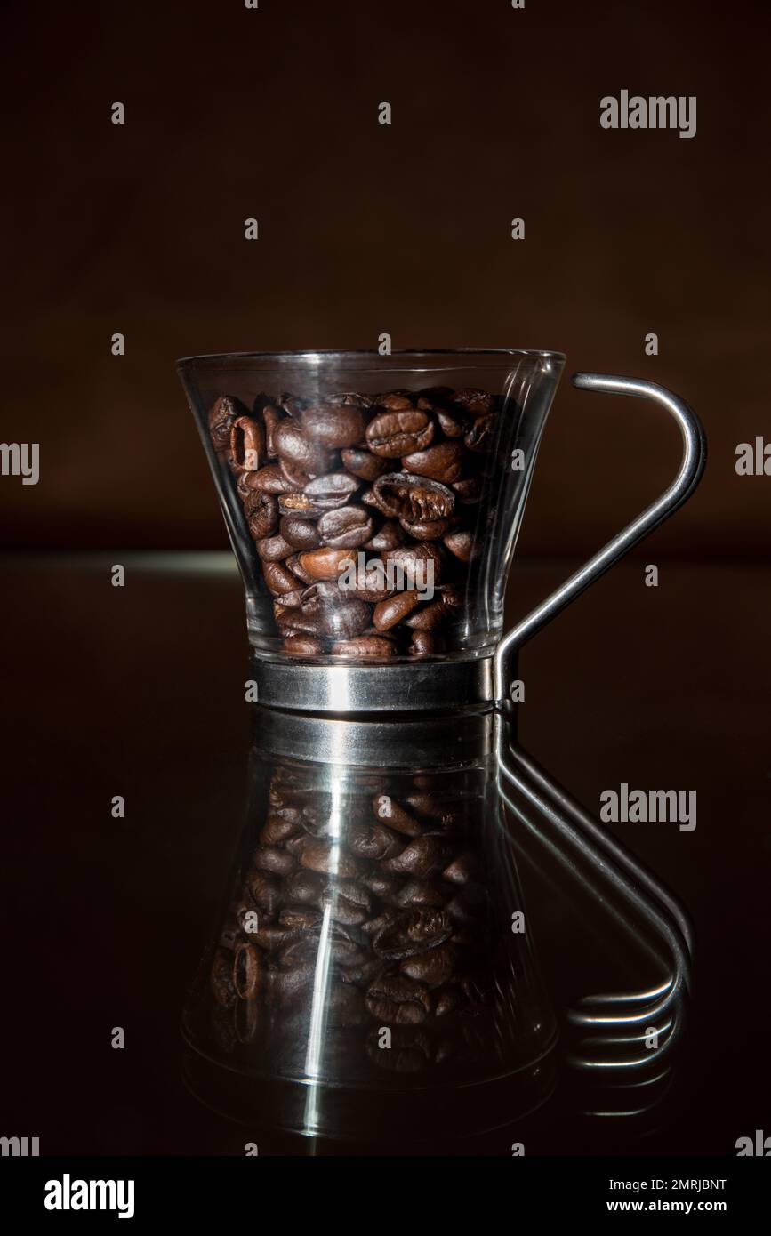A glass cup full of coffee beans fon brown surface with a copy space ...