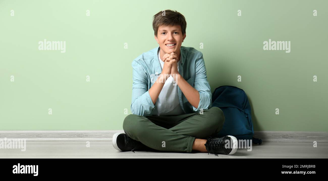 Teenage boy with backpack sitting on floor near green wall Stock Photo ...