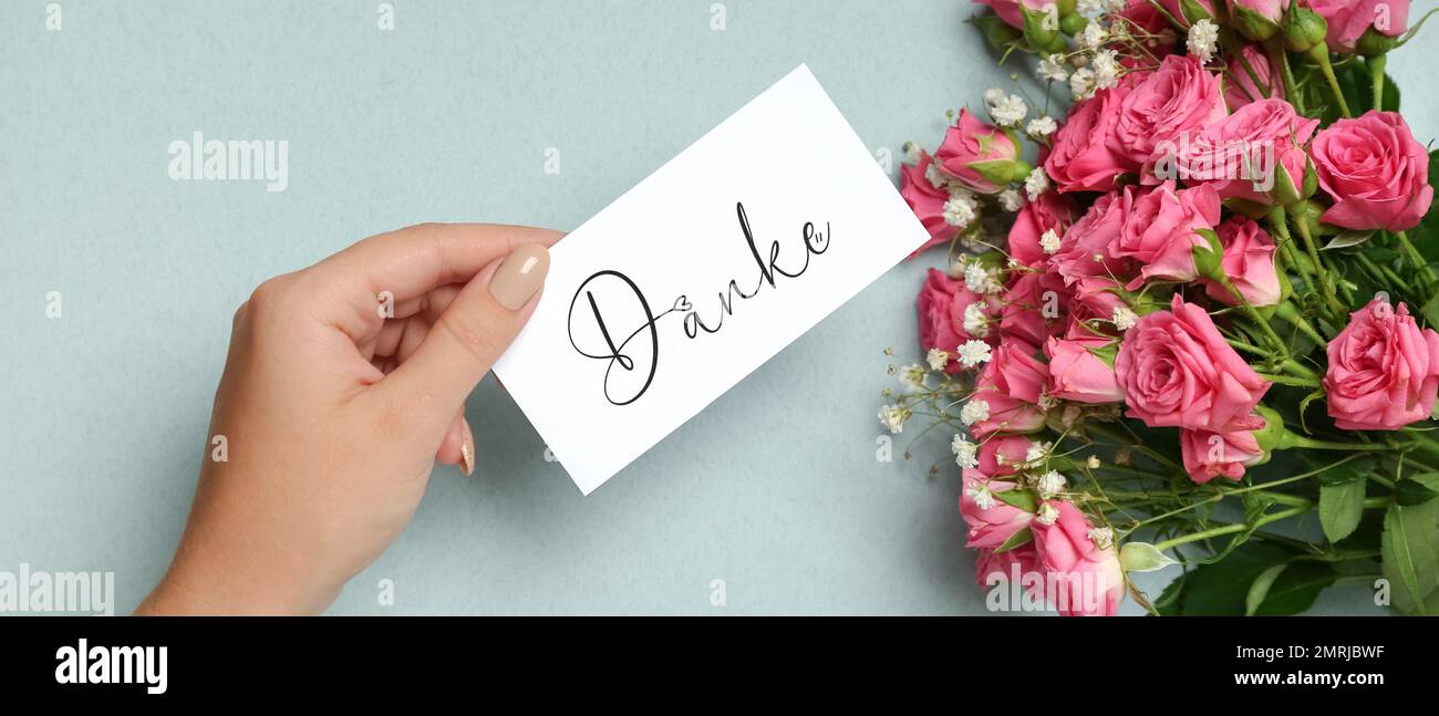 Female hand holding card with word DANKE and beautiful bouquet on grey ...