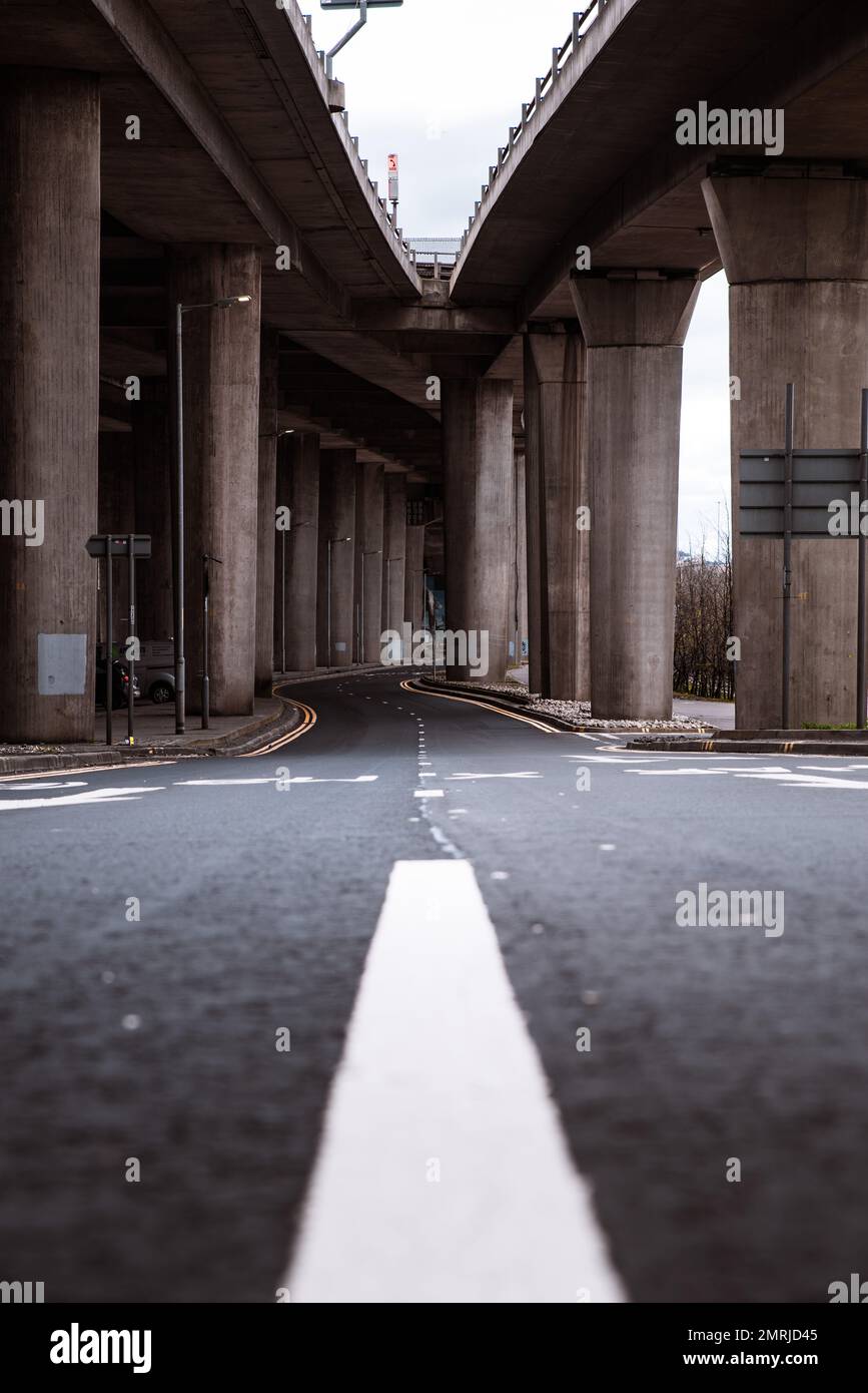An asphalt road under concrete urban bridge pilars and light sky ...