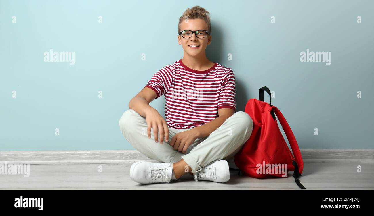 Teenage boy with backpack sitting on floor near grey wall Stock Photo ...